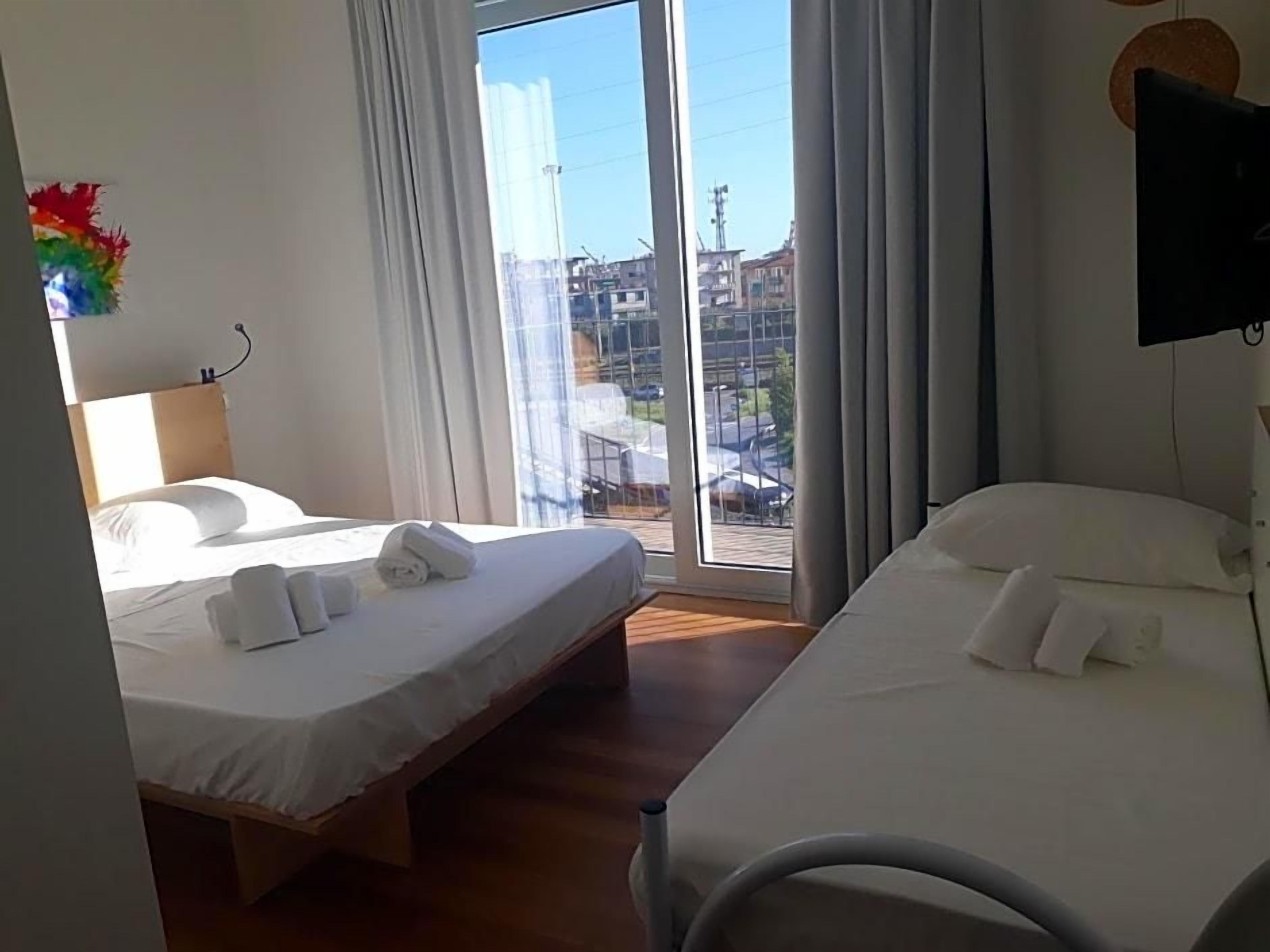 Quarto de hotel com duas camas, uma janela grande com cortinas, televisão de tela plana e vista para a paisagem urbana.