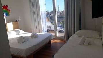 Quarto de hotel com duas camas, uma janela grande com cortinas, televisão de tela plana e vista para a paisagem urbana.