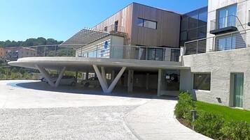 Um edifício moderno com entrada coberta, área de estacionamento e jardim ajardinado.