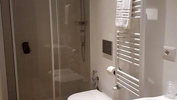Casa de banho com cabine de duche em vidro, lavatório branco e suporte para toalhas.
