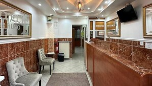 Um saguão de hotel com paredes de mármore, área de estar, balcão de recepção e uma televisão na parede.