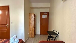 Quarto de hotel com duas camas, um guarda-roupa de madeira, uma mesa pequena e uma porta com um mural.