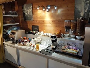 Uma mesa de buffet com diversos alimentos, uma máquina de café e um jarro de café.
