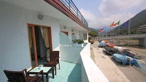 Uma varanda com mesa e cadeiras, vista para o mar e bandeiras ao fundo.