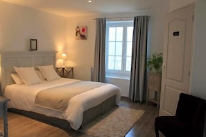 Quarto com cama, mesas de cabeceira, janela com cortinas, uma planta e uma porta.