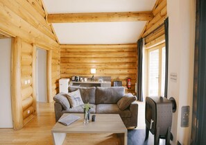 Interior de cabana de troncos com sala de estar, sofá, mesa de centro, lareira e cozinha.
