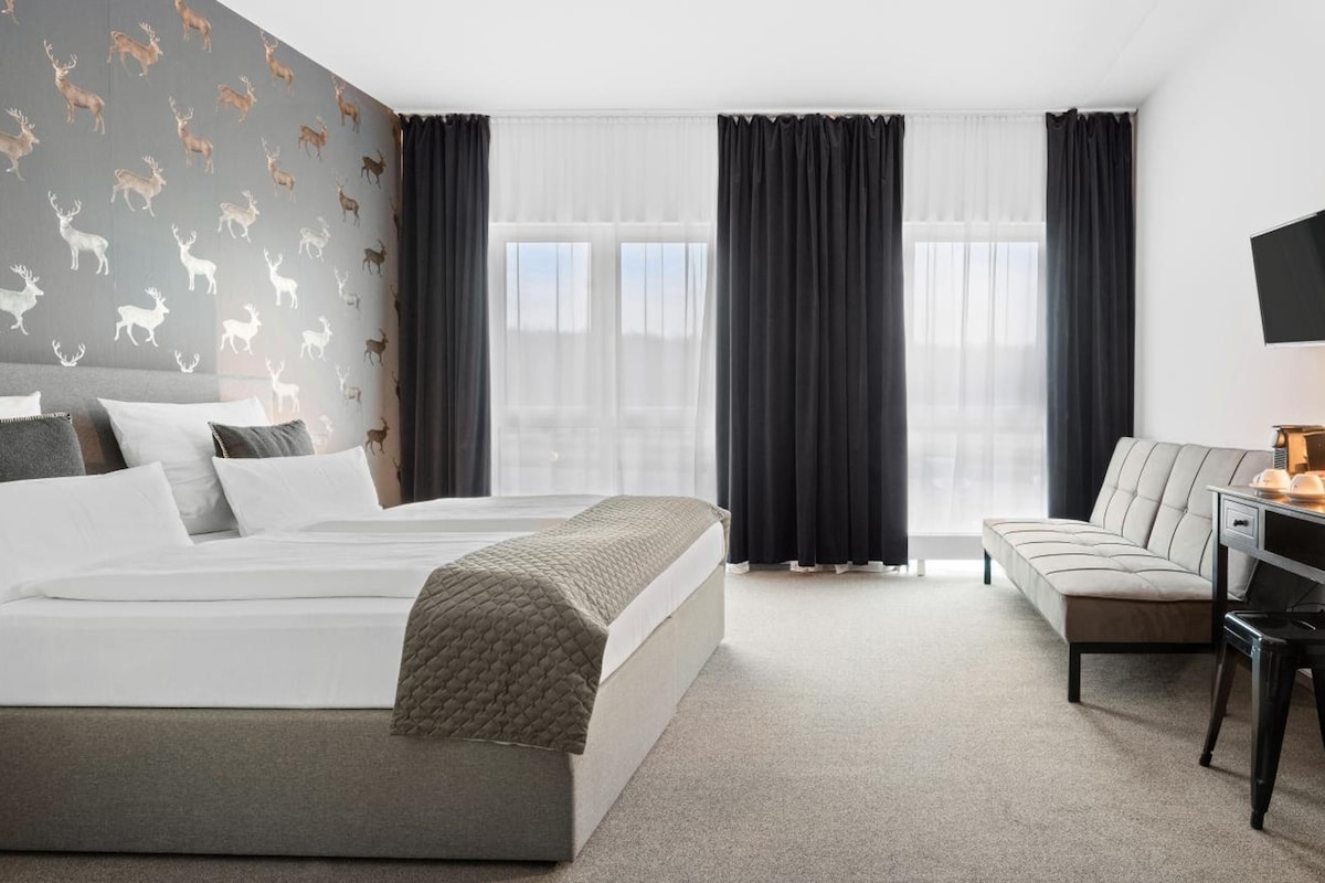 Quarto de hotel com cama, escrivaninha, cadeira, televisão e janela com cortinas.