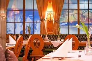 Uma sala de jantar com cadeiras de madeira, uma mesa posta com toalha branca e vista através de grandes janelas.