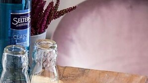 Uma mesa de madeira com uma garrafa, dois copos e um pequeno recipiente.