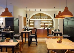 Restaurante com balcão central, várias mesas e luminárias pendentes.