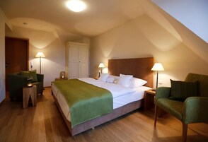 Quarto de hotel com cama, duas cadeiras, piso de madeira e porta.