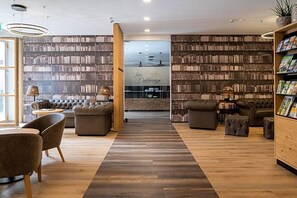 Uma biblioteca moderna com estantes, sofás de couro e um corredor central.