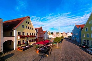 Rua de paralelepípedos com edifícios tradicionais europeus, um guarda-chuva vermelho e um céu azul límpido.
