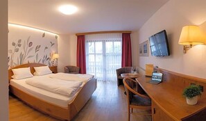 Quarto de hotel com cama, escrivaninha, cadeira, televisão e janela com cortinas.