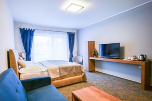 Quarto de hotel com cama, televisão, sofá e mesa de centro.
