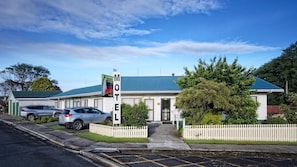 Um motel com teto verde, cerca branca de piquete e uma placa.