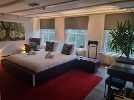 Quarto moderno com cama grande, tapete vermelho, escrivaninha e planta em vaso.