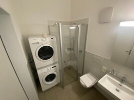 Casa de banho compacta com máquina de lavar roupa, cabine de duche e lavatório.