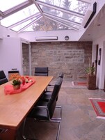 Uma sala de conferências com uma mesa comprida, cadeiras pretas, parede de pedra e teto de vidro.