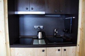 Cozinha compacta com pia, chaleira e torneira, e armários de madeira.