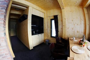 Interior em madeira com cozinha, mesa de jantar e cadeiras, e uma janela.