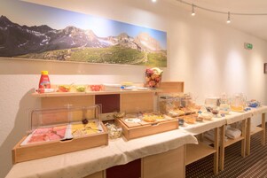 Disposição de buffet com diversos alimentos e uma pintura da paisagem de montanhas na parede.