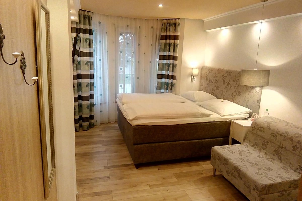 Quarto com cama, mesa de cabeceira, cadeira e luminária fixada na parede.