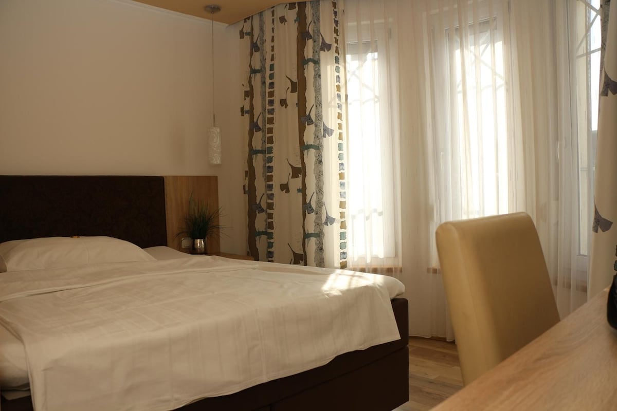 Quarto de hotel com cama, cadeira e janela com cortinas.