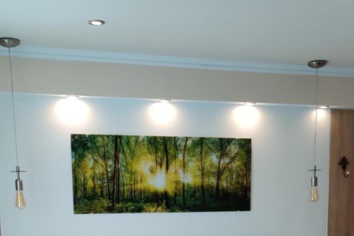 Uma cama bem arrumada com cabeceira verde, um quadro de uma floresta na parede e piso de madeira.