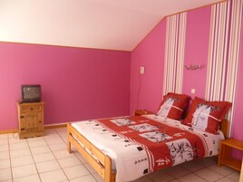 Quarto com cama, mesa de cabeceira de madeira, televisão em um móvel e cortina listrada.