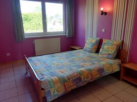 Quarto com cama, janela, radiador e luminária fixada na parede.