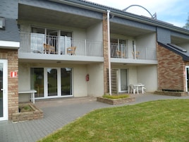 Um edifício residencial de dois andares com varanda, detector de incêndio e pequena área de estar ao ar livre.