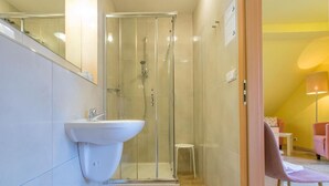 Uma casa de banho moderna com cabine de duche de vidro, lavatório branco e um pequeno banquinho.