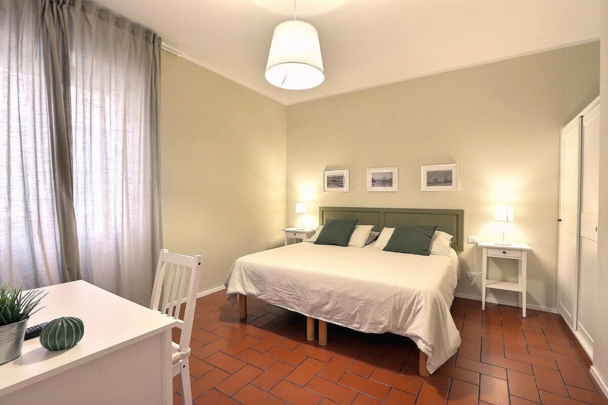 Quarto com cama, mesas de cabeceira, escrivaninha e uma cadeira.