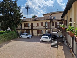 Um pátio com área pavimentada, dois carros brancos estacionados, uma escadaria e um edifício com várias janelas e sacadas.