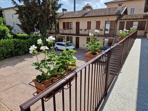 Varanda com plantas em vasos e um carro branco estacionado ao fundo.