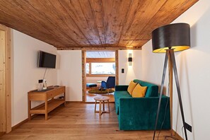 Quarto com teto de madeira, sofá verde, televisão, escrivaninha e abajur.