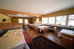 Restaurante com várias mesas e cabines, piso de madeira e amplas janelas que permitem entrada de luz natural.