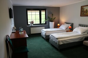 Quarto de hotel com duas camas de solteiro, uma escrivaninha com cadeira, radiador, janela com vista e um quadro na parede.