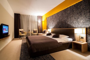 Quarto de hotel com cama, televisão, duas cadeiras, abajur e parede com padrão de zebra.