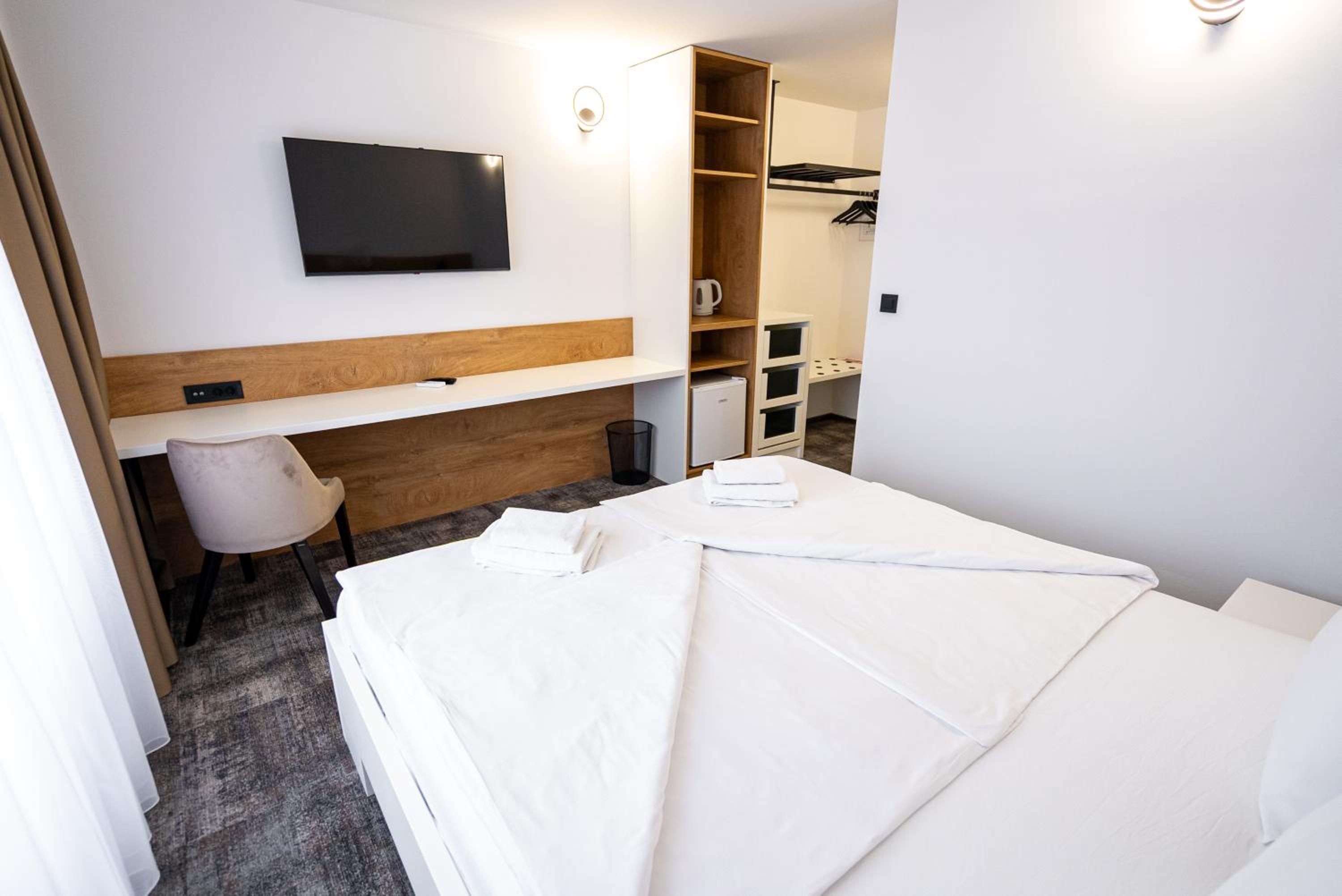 Quarto de hotel com cama, televisão na parede, guarda-roupa e um pequeno espaço de estar.
