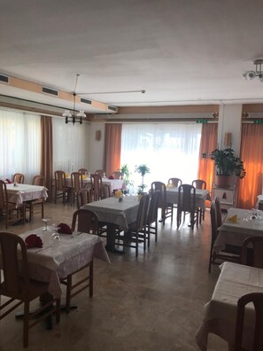 Uma sala de jantar com várias mesas e cadeiras, aparelhos de ar condicionado e um ventilador de teto.