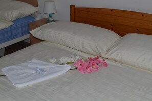 Quarto de hotel com cabeceira de madeira, cama com roupa de cama branca, colcha azul, toalha branca e flores cor-de-rosa sobre a cama.