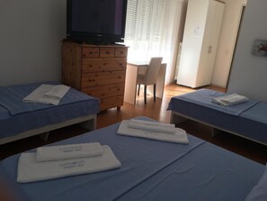 Quarto de hotel com duas camas, uma televisão sobre uma cômoda de madeira, uma escrivaninha e uma cadeira.