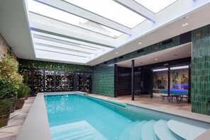 Uma área interna de piscina moderna com teto skylight, piscina com degraus de acesso e porta de vidro que dá para área externa.