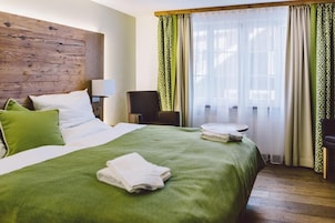 Quarto de hotel com uma cama grande, uma cadeira, uma mesa pequena e uma janela com cortinas.