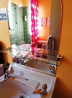 Casa de banho com lavatório envidraçado, chuveiro com parede em azulejo verde e cortina rosa.