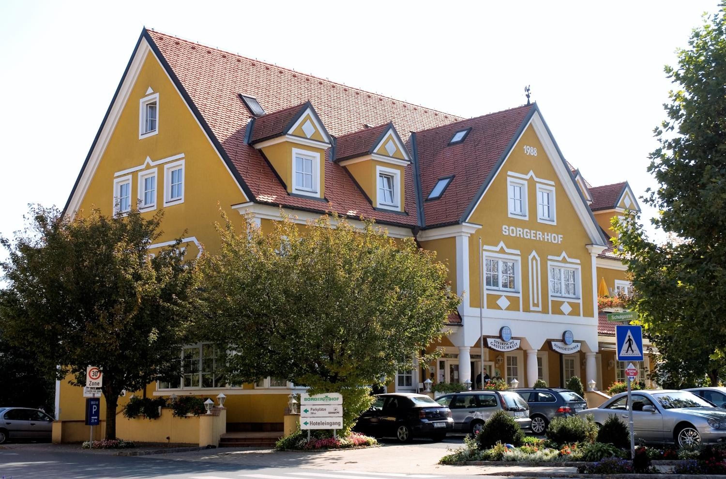 Um edifício amarelo com telhado vermelho, identificado como 'SORGER-HOF', apresenta estilo arquitetônico tradicional com várias janelas e uma entrada central.