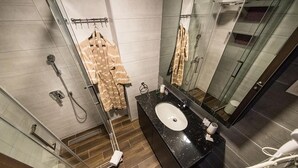 Casa de banho moderna com cabine de duche em vidro, lavatório em mármore preto e toalheiro com toalhas riscadas.