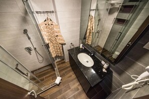 Casa de banho moderna com cabine de duche em vidro, lavatório em mármore preto e toalheiro com toalhas riscadas.